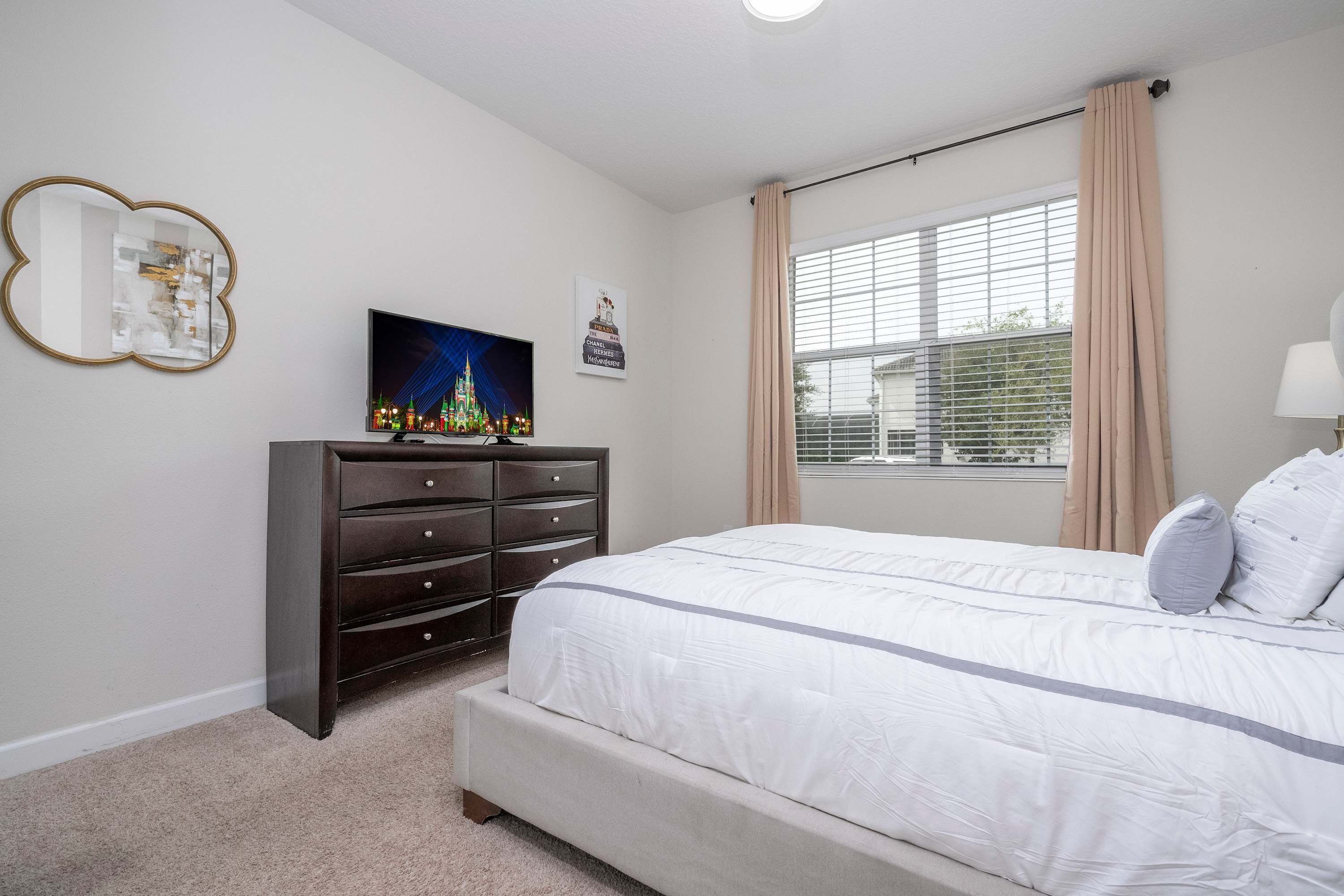 Quarto com cama, penteadeira, televisão e janela com cortinas.
