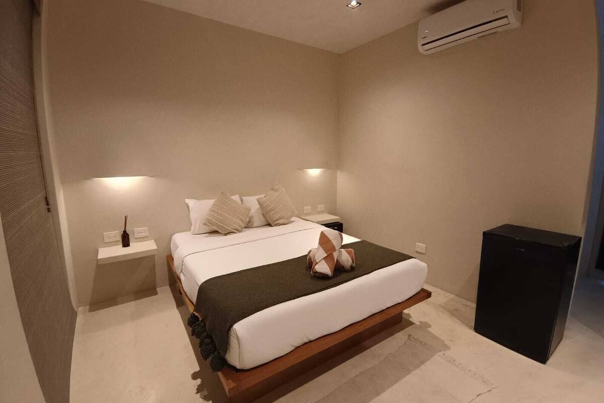 Quarto com cama, mesas de cabeceira, ar condicionado e um objeto preto no chão.