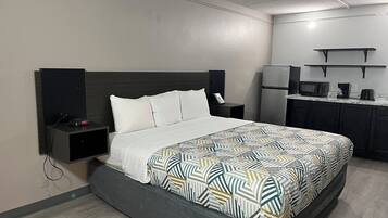 Quarto de hotel moderno com cama, mesa de cabeceira, escrivaninha, micro-ondas, frigorífico e máquina de café.