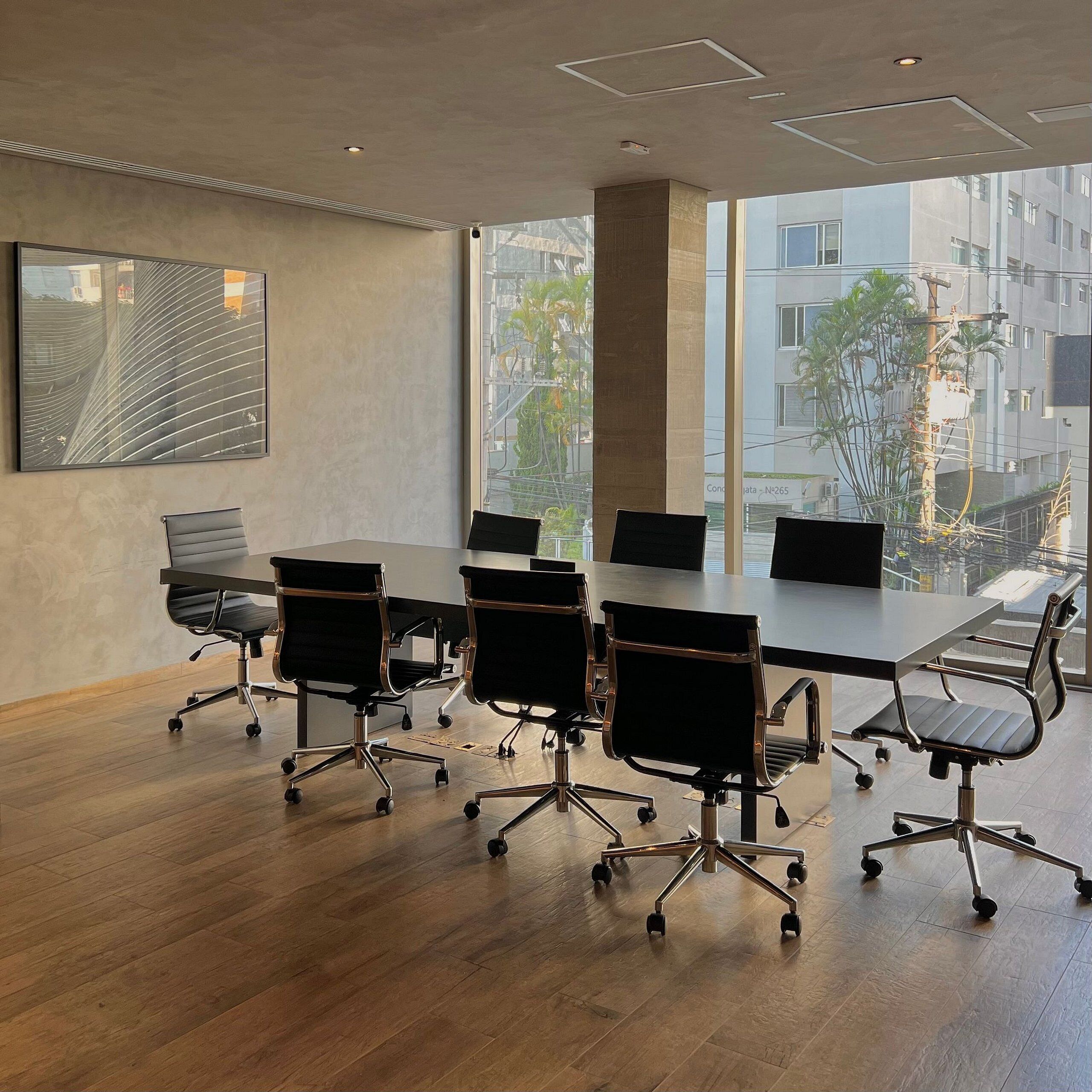 Uma sala de conferências com uma mesa grande, seis cadeiras de escritório pretas e uma janela ampla com vista para a cidade.