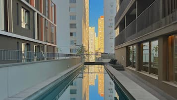 Um edifício moderno com uma piscina refletora em primeiro plano, rodeado por apartamentos altos.