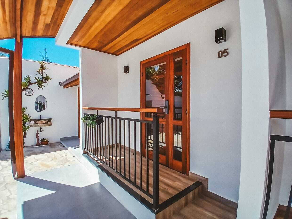Um edifício moderno com escadaria de madeira, pequena área externa com plantas e uma porta com o número 05.