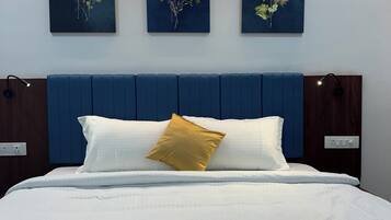 Uma cama com roupa de cama branca e dourada, uma cabeceira azul e três quadros florais na parede.