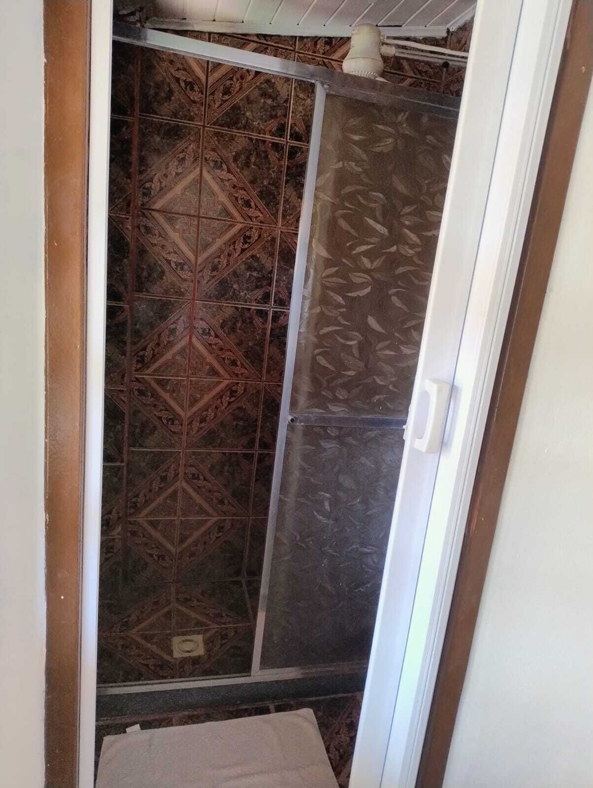 Quarto com porta deslizante que dá para um banheiro. O banheiro possui um painel de azulejos estampados e um box com porta de vidro.