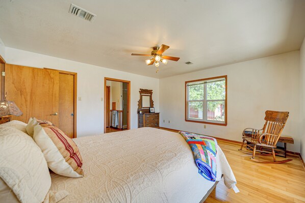 Quarto com cama grande, piso de madeira, ventilador de teto, janela e cadeira de balanço.