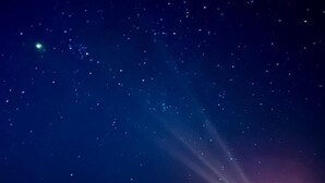 Cena noturna no deserto com céu estrelado e límpido, uma tenda com mesa e cadeiras, e uma estrutura iluminada ao fundo.