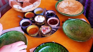 Uma mesa redonda de madeira com diversos alimentos e recipientes, sobre um sofá colorido com estampas listradas.