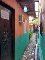 Um corredor estreito com piso de azulejos, uma placa indicando 'Suite 3 Familiar Com Cozinha' e um aparelho de ar condicionado na parede.