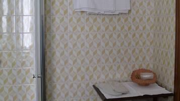 Casa de banho com azulejos estampados, divisória de chuveiro em vidro, porta-toalhas com toalhas dobradas e uma prateleira com toalhas dobradas e um saboneteiro.