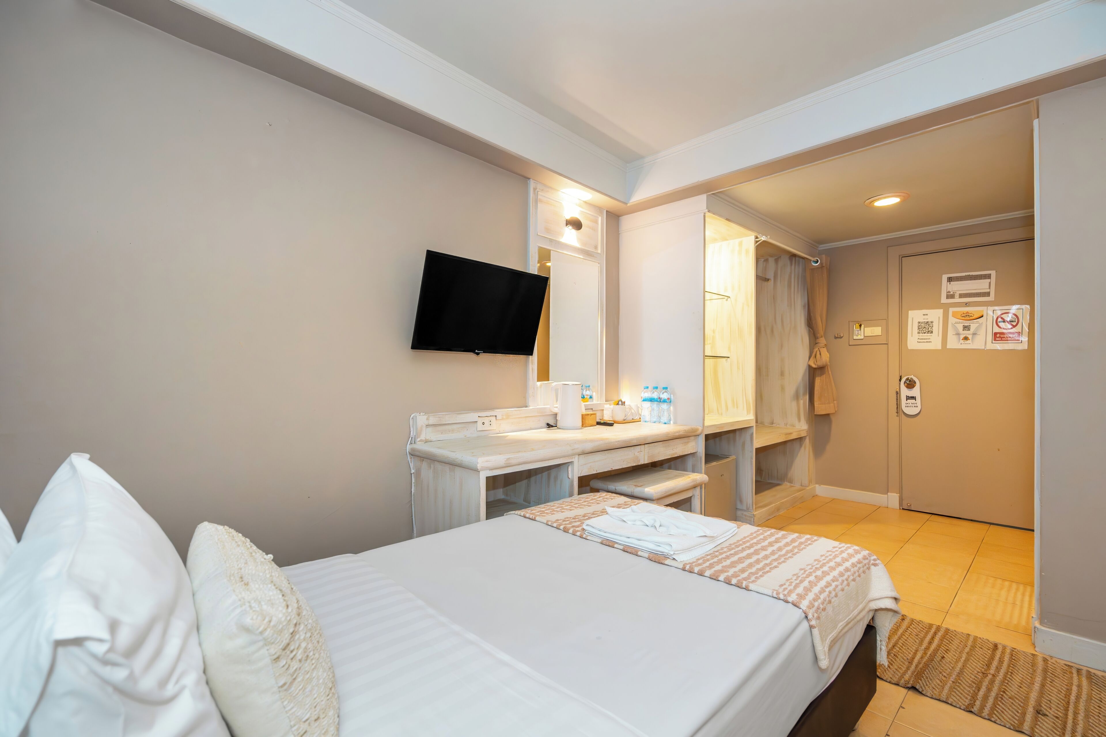 Quarto de hotel com cama, escrivaninha com espelho, televisão e porta com aviso.