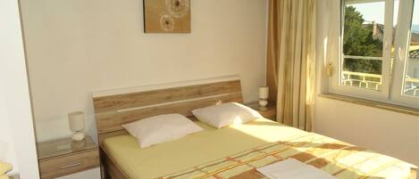 Um quarto com cabeceira de madeira, cama com colcha listrada, mesa de cabeceira com abajur e janela com cortinas.