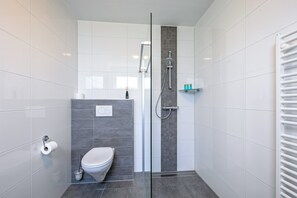 Casa de banho moderna com cabine de chuveiro em vidro, sanita e suporte para toalhas.