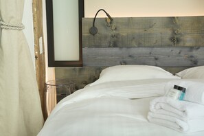 Cama bem arrumada com lençóis brancos e uma toalha dobrada ao lado.
