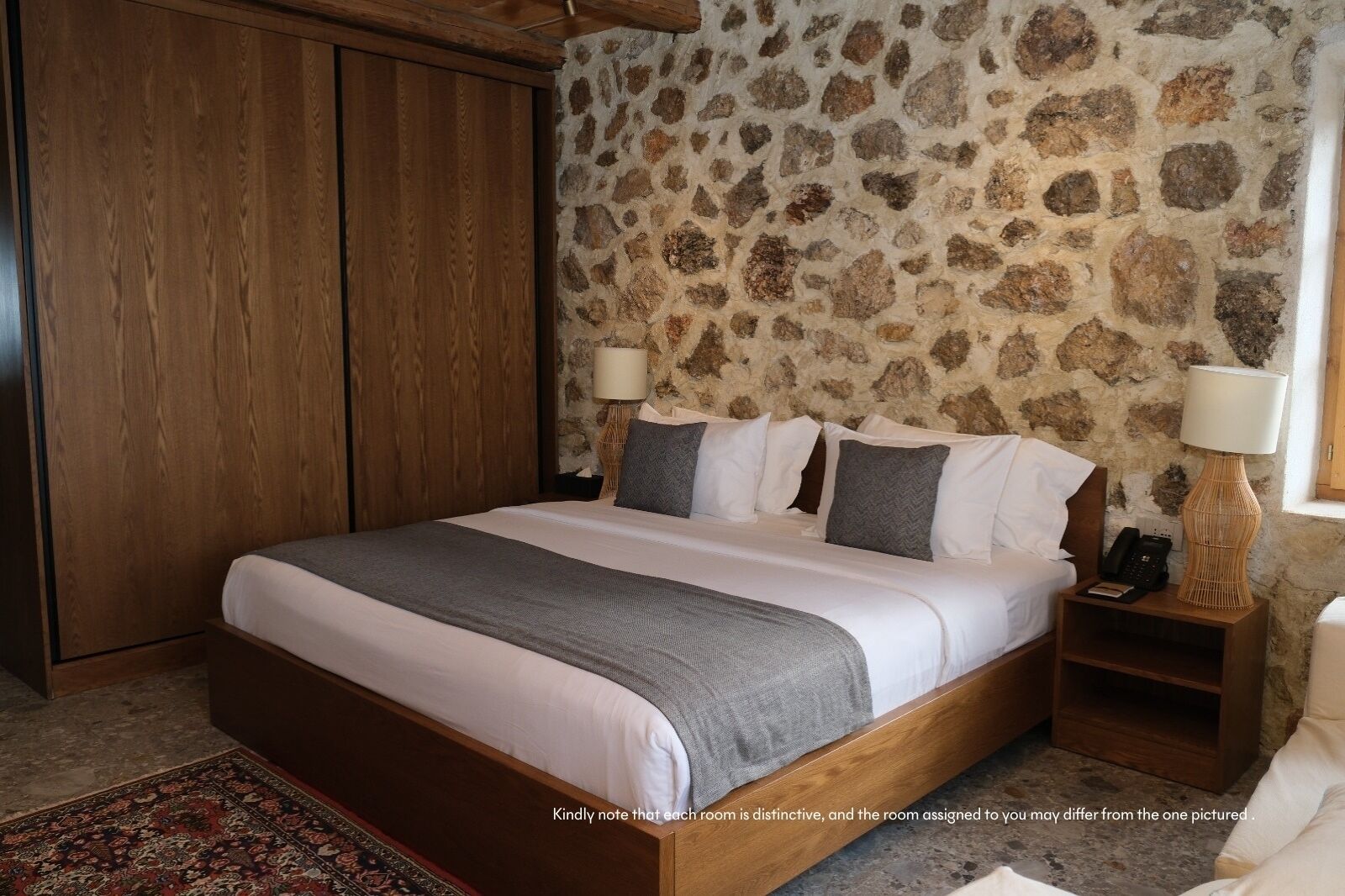 Quarto com parede de pedra, estrutura de cama de madeira e mesa de cabeceira com abajur.