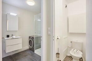 Casa de banho moderna com cabine de duche em vidro, lavatório branco com toalha e sanita com dois rolos de papel higiénico.