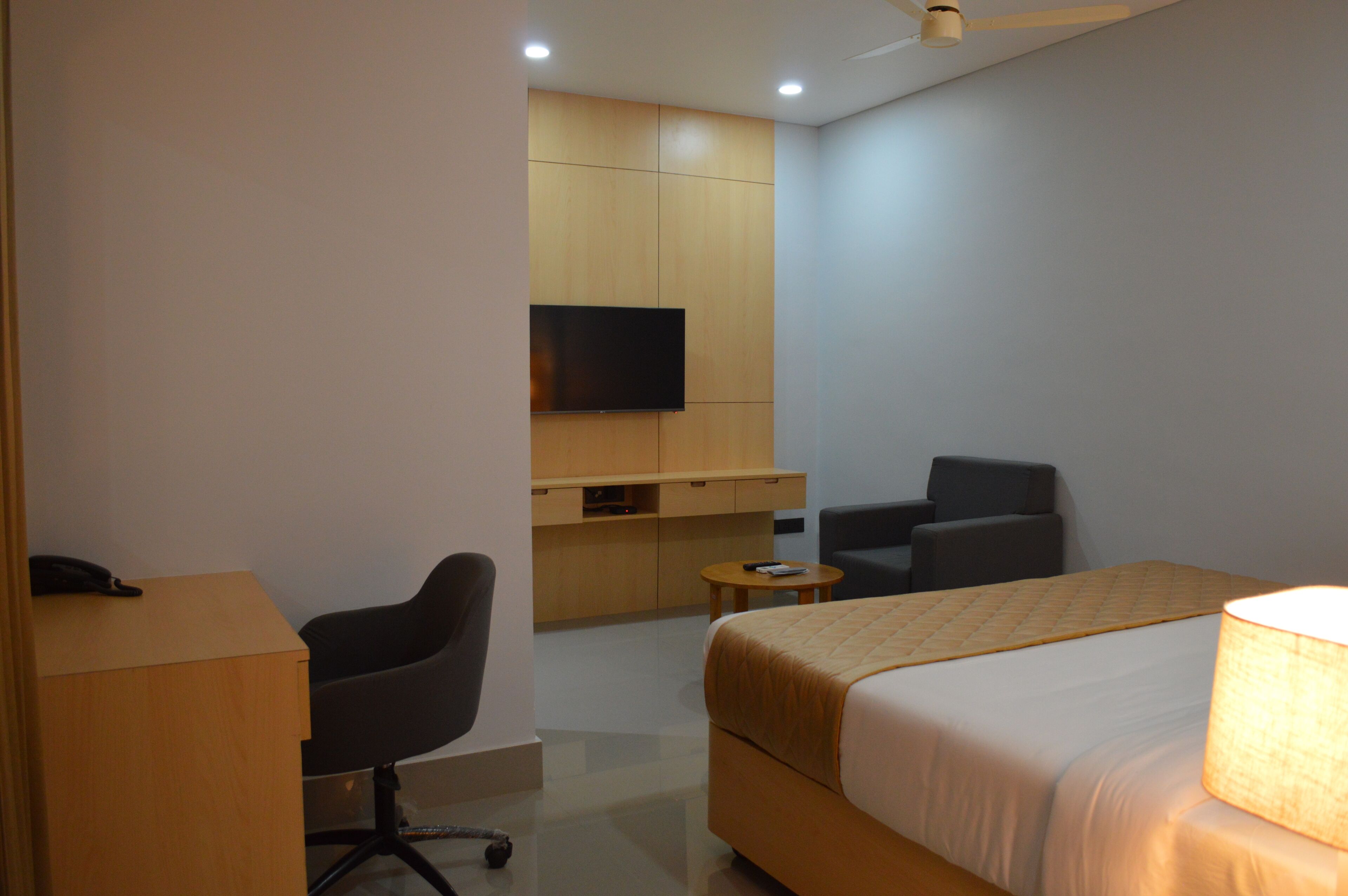 Quarto de hotel com uma cama, escrivaninha, cadeira, televisão e uma mesinha.