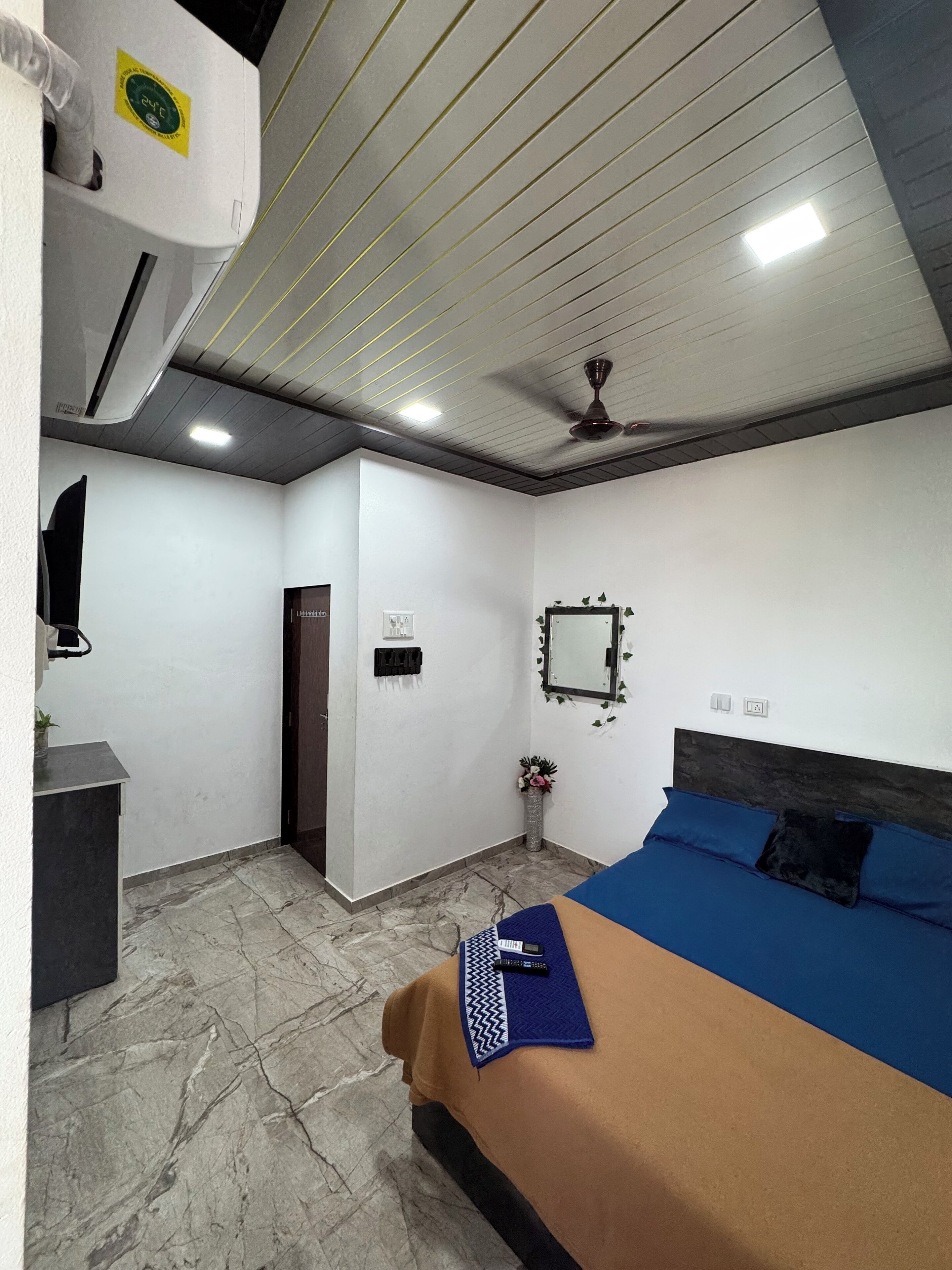 Quarto de hotel com cama, escrivaninha, espelho, ventilador de teto e porta.