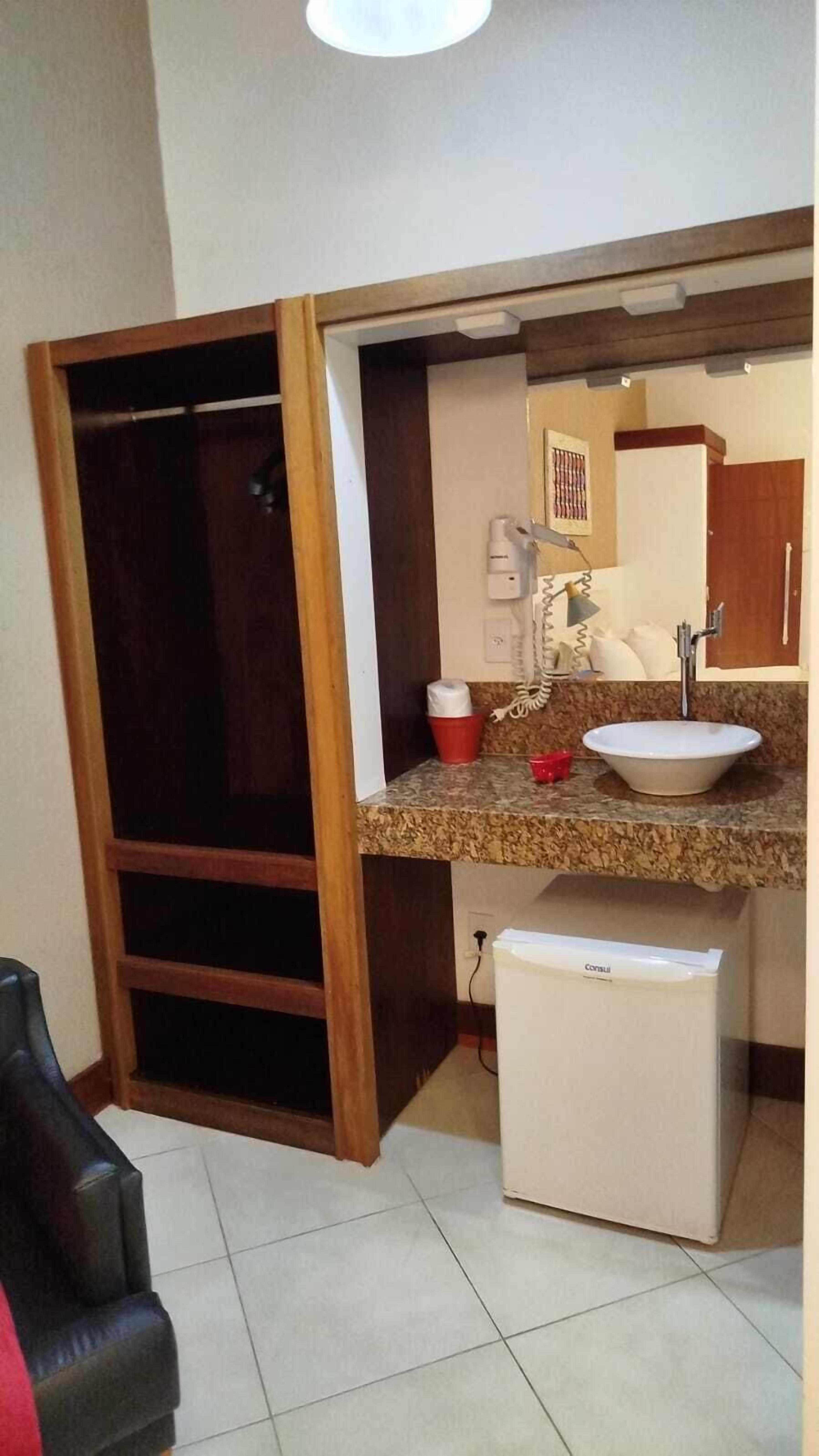 Casa de banho com porta de madeira, pia, espelho e um pequeno frigorífico.