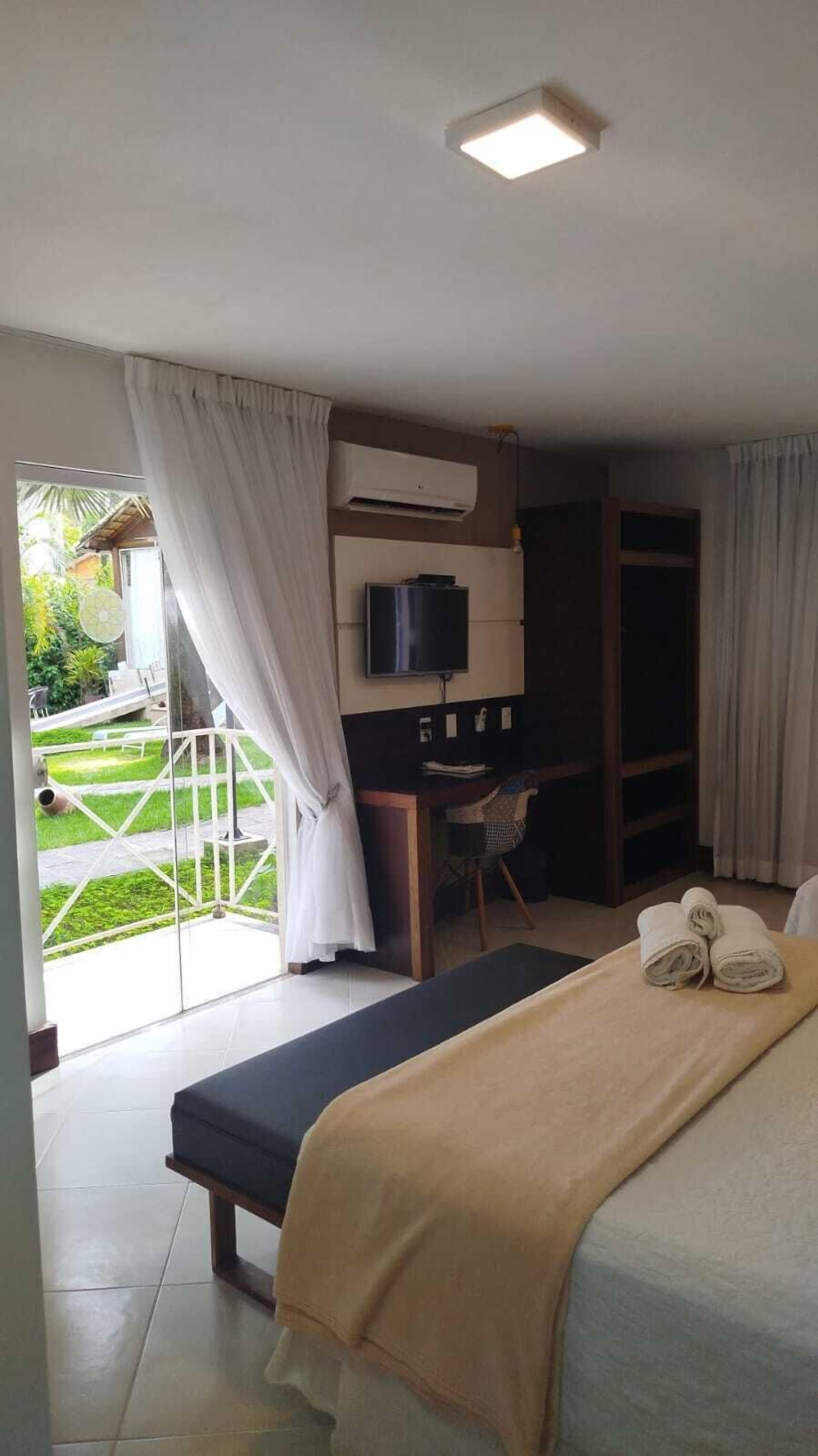 Quarto de hotel com cama, escrivaninha, televisão e vista para um jardim.