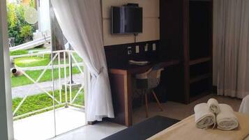 Quarto de hotel com cama, escrivaninha, televisão e vista para um jardim.