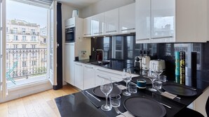 Cozinha moderna com armários brancos, bancada preta e um espaço de refeições preparado para quatro pessoas.