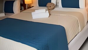 Cama bem arrumada com roupa de cama azul e branca, cabeceira de madeira e um tapete redondo pequeno.