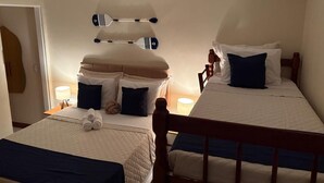 Quarto de hotel com duas camas, cada uma com cabeceira de madeira, uma mesinha de cabeceira com abajur e um porta-toalhas fixado na parede.