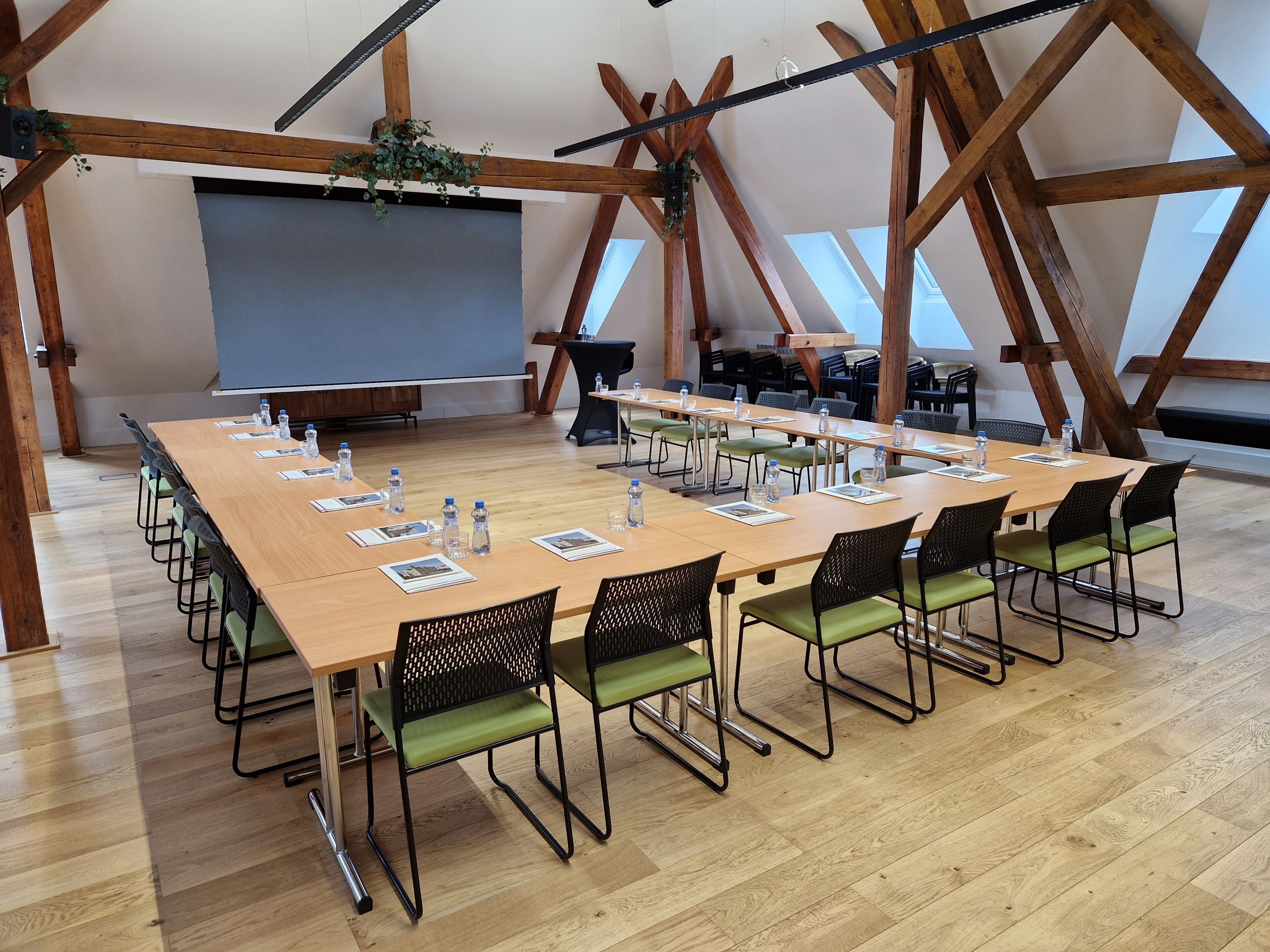 Uma sala de conferências com uma mesa comprida, cadeiras, garrafas de água e uma tela de projetor.