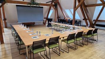 Uma sala de conferências com uma mesa comprida, cadeiras, garrafas de água e uma tela de projetor.