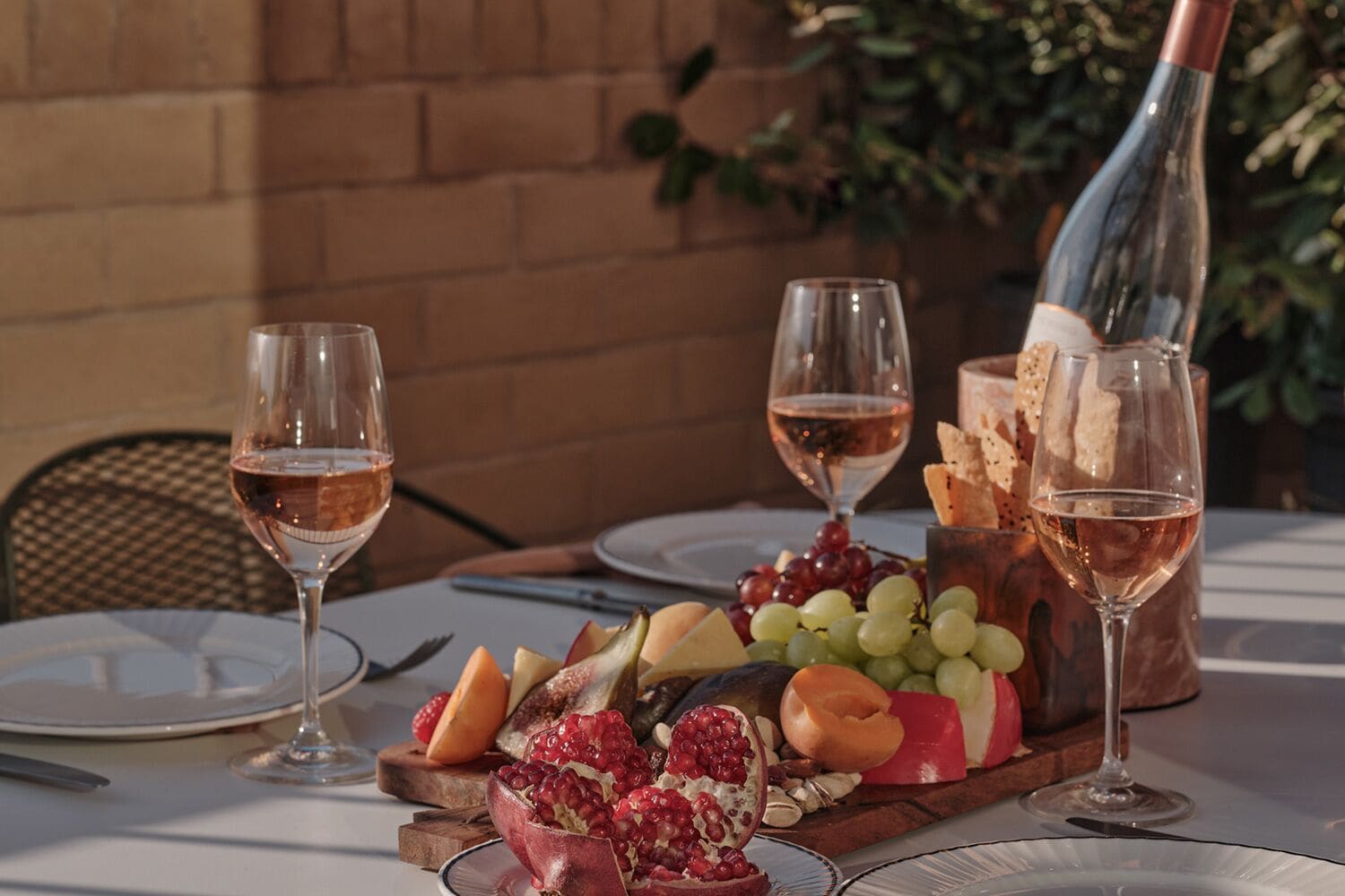 Uma mesa posta para refeição, com copos de vinho, tábua de queijos e uma garrafa de vinho.