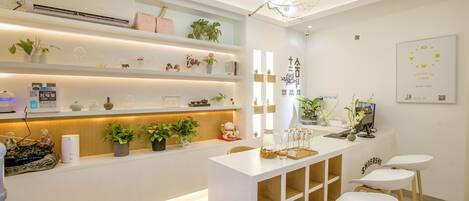 Uma área de recepção moderna, com um balcão branco, várias prateleiras com objetos decorativos e um design limpo e minimalista.