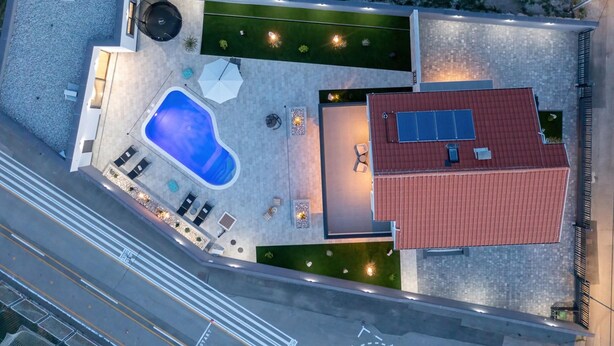 Vista aérea de uma propriedade residencial moderna com piscina, área de estar externa e um edifício equipado com painéis solares.