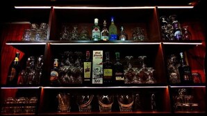 Uma área de bar com prateleiras cheias de garrafas de bebidas e copos.
