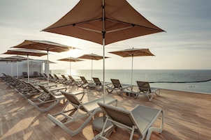 Um deck ensolarado com cadeiras de lounge e guarda-sóis com vista para o mar.