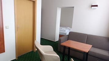 Um quarto com porta de madeira, tapete verde, sofá cinzento, uma mesa pequena e uma cadeira.