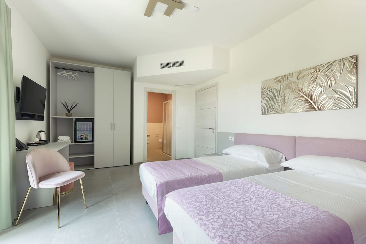 Quarto de hotel com duas camas, televisão, escrivaninha e guarda-roupa.
