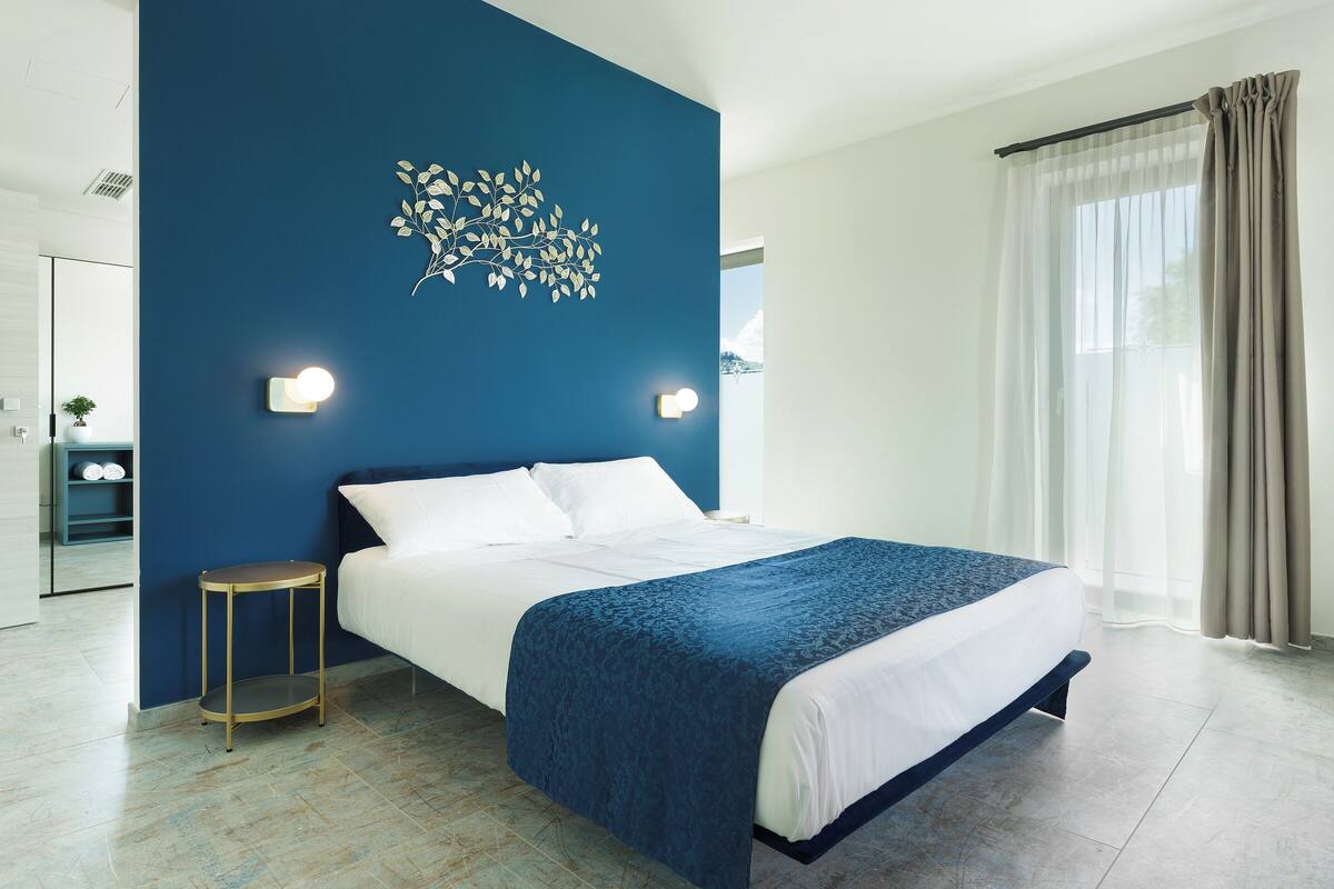 Quarto de hotel moderno com uma cama grande, uma mesinha de cabeceira e um detalhe decorativo na parede.