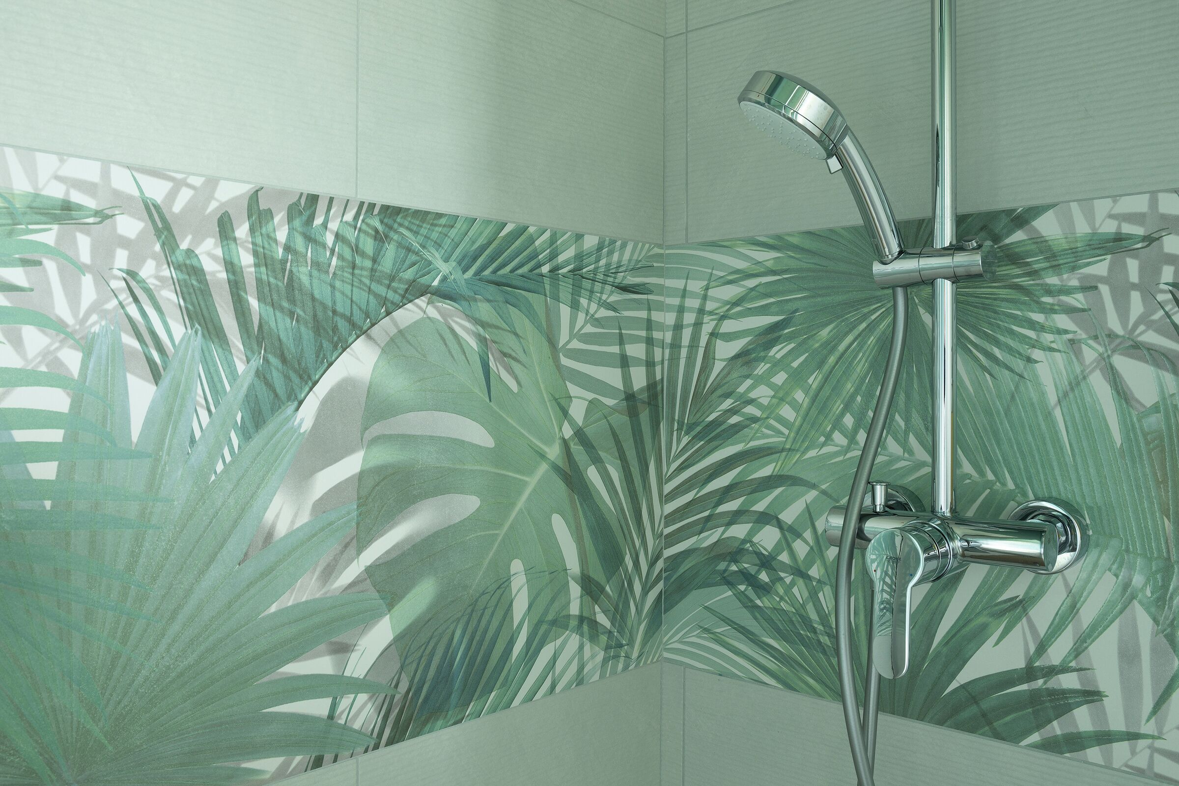 Um chuveiro com uma torneira cromada moderna e um painel de vidro com padrão de folha tropical.