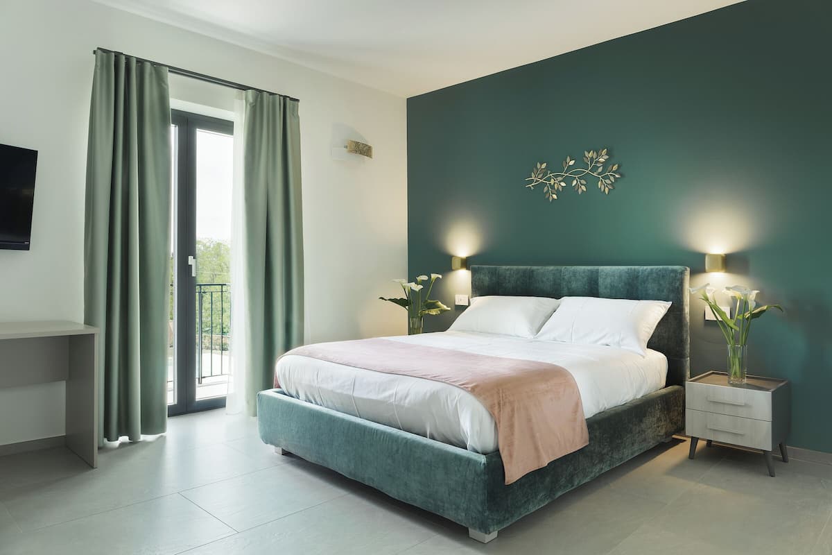 Quarto com cama, mesas de cabeceira, televisão e vista para o exterior.