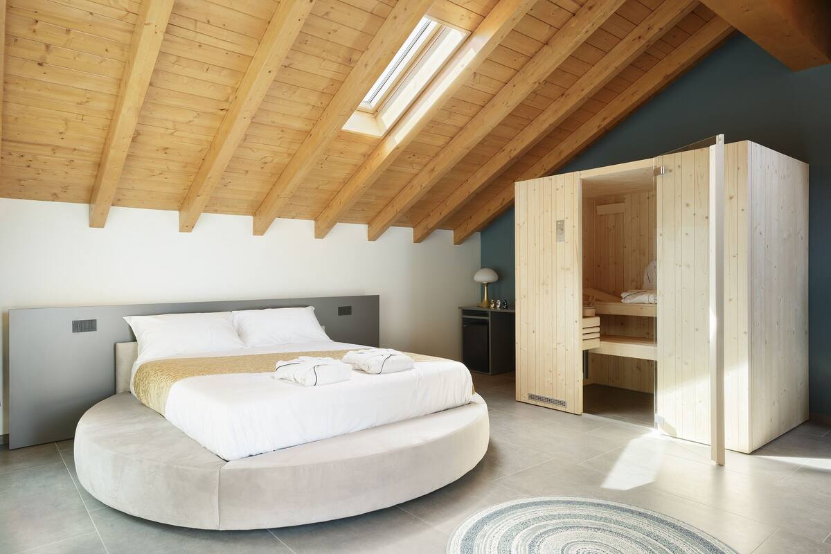 Quarto moderno com cama curva, vigas de madeira no teto e armário embutido de madeira.