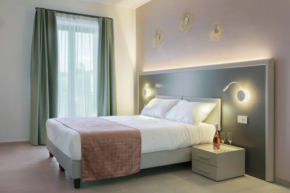 Quarto de hotel moderno com cama, mesa de cabeceira e luminária fixada na parede.