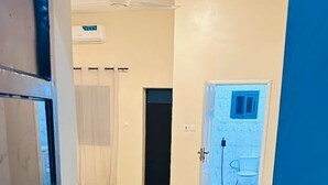 Quarto de hotel com cama, banheiro com vaso sanitário e chuveiro, e porta que dá para outro cômodo.