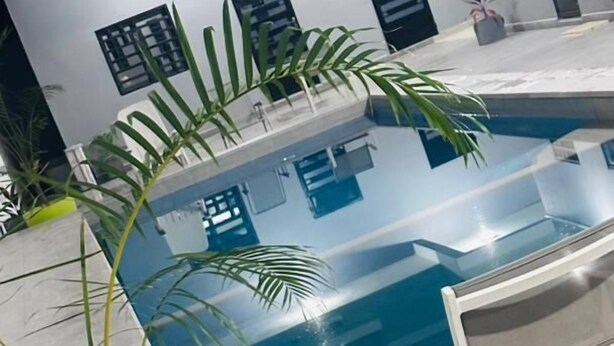 Uma área interna de piscina moderna, piscina azul cristalina, uma cadeira branca e uma planta verde brilhante em vaso.