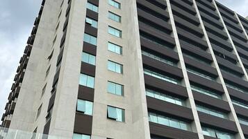 Um edifício alto com design arquitetônico moderno, apresentando uma combinação de fachadas de concreto e vidro, várias sacadas e uma entrada de vidro refletivo.