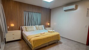Quarto moderno com cama, mesas de cabeceira, luminária no teto e ar condicionado.