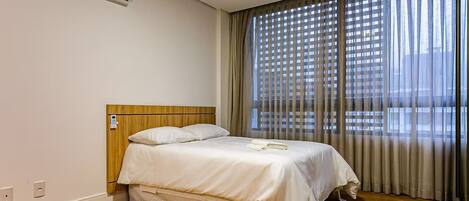 Quarto de hotel com cama, painel de controle e janela com cortinas.