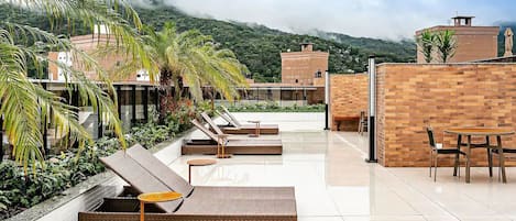 Terraço no telhado com cadeiras de descanso, uma mesa de jantar e vista para uma paisagem montanhosa.