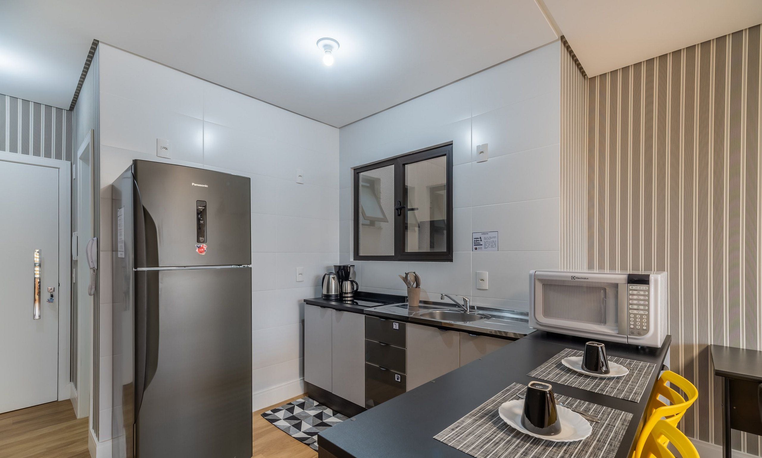 Cozinha moderna com geladeira, micro-ondas e área de jantar com mesa e cadeiras.