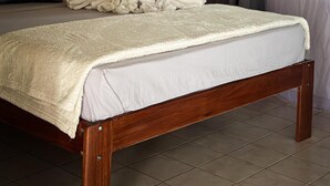 Uma cama bem arrumada com toalhas dispostas em formato de coração, um cobertor branco e fofo e uma cabeceira de madeira.