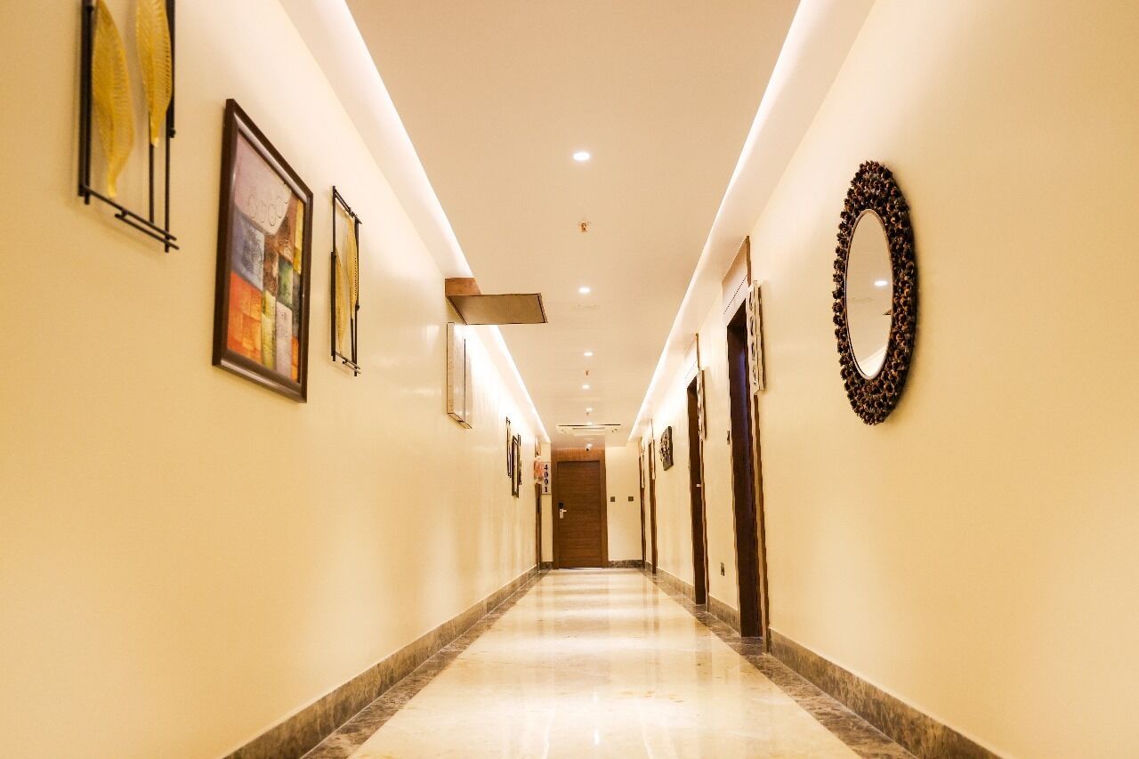 Corredor de hotel com obras de arte emolduradas nas paredes, piso de mármore e porta de madeira no final.